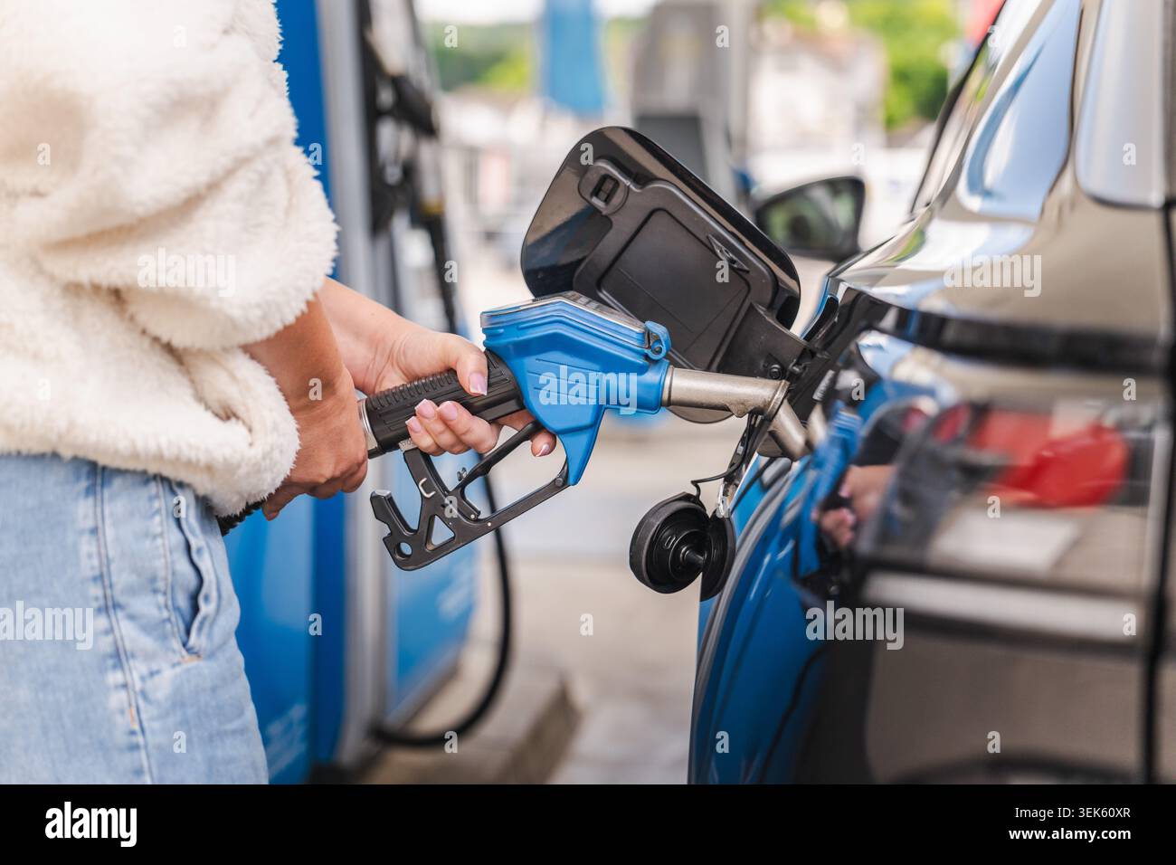 Woman refueling black automobile at gas station with blue fuel pump ...