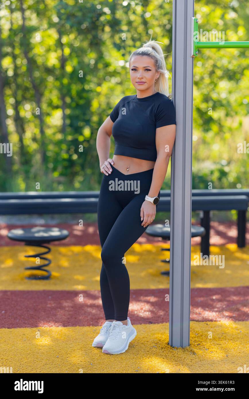 A woman in athletic attire stands at an outdoor gym, showcasing ...