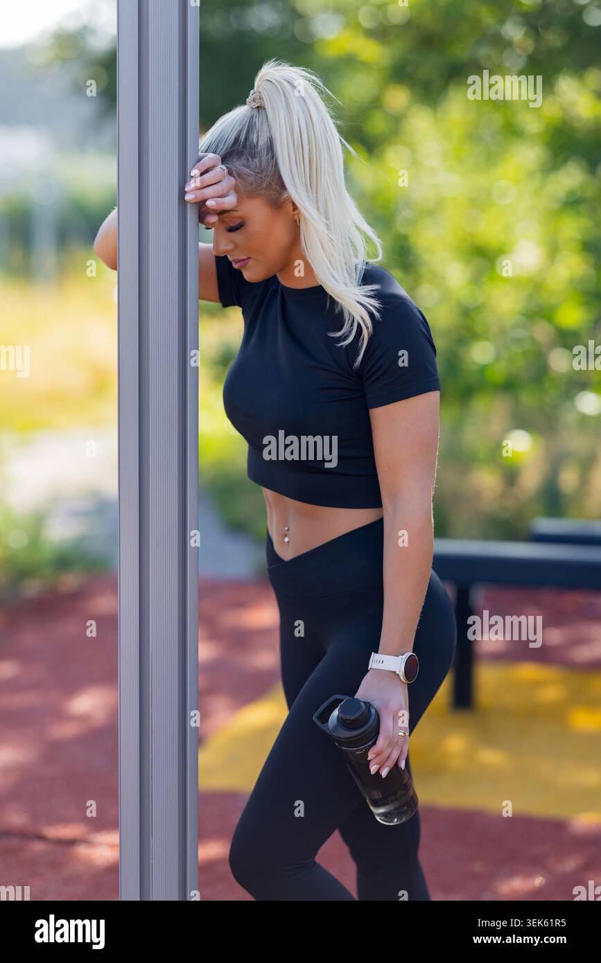 Active woman taking a break during an outdoor workout, dressed in ...