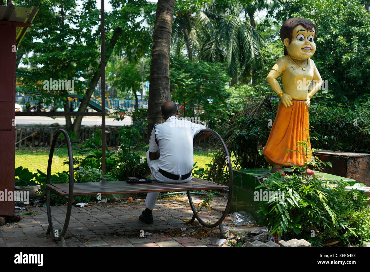 A policeman rests on a bench under shadow of trees on a hot summer day ...