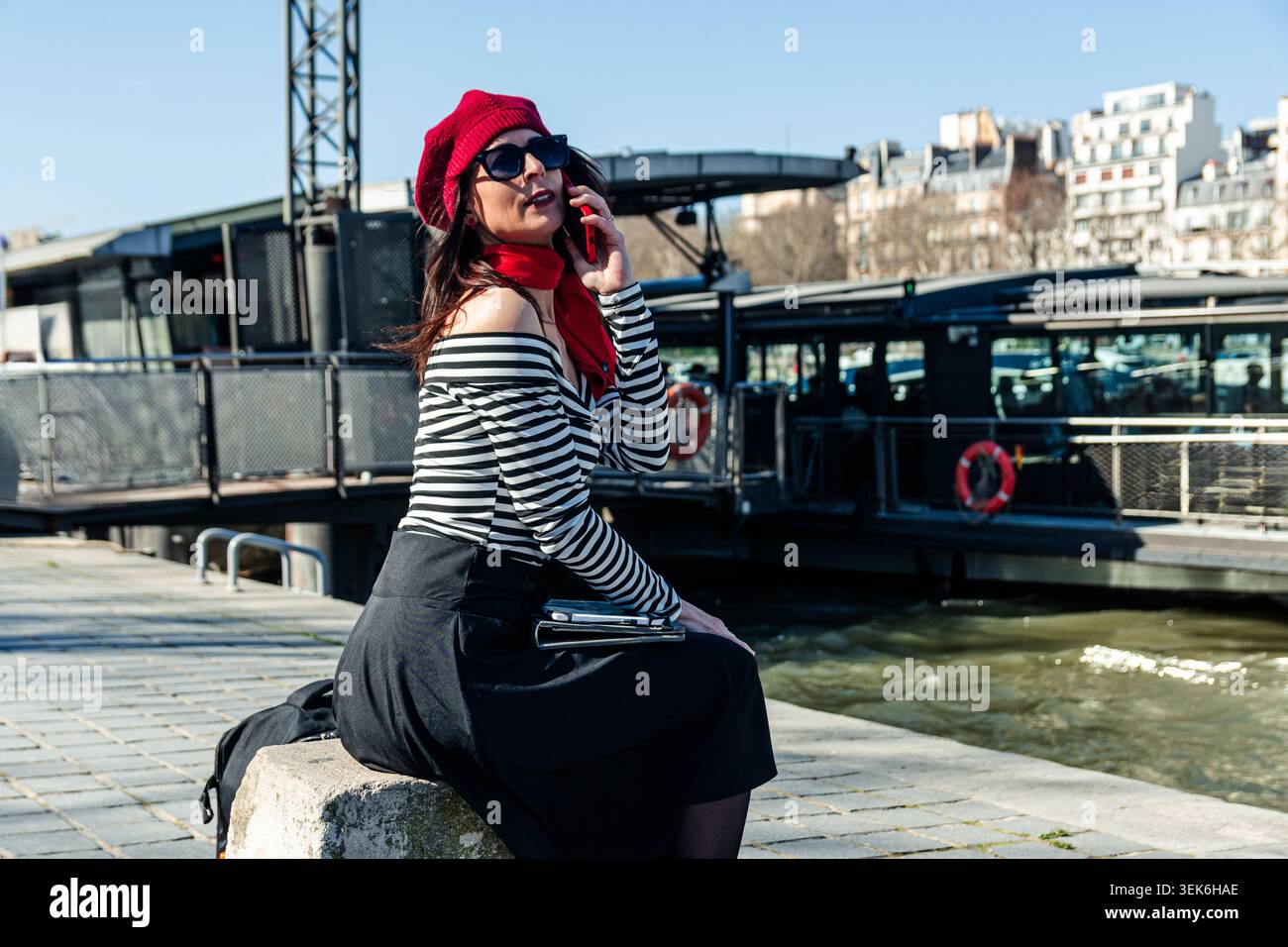 Woman in french style clothing sitting by the seine river and using a ...