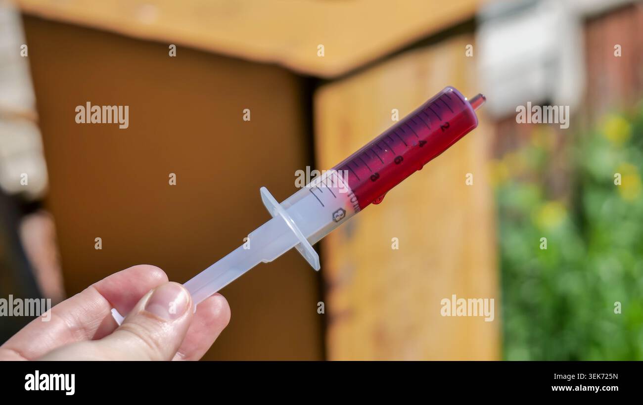 Hand holding syringe with red liquid Stock Photo - Alamy