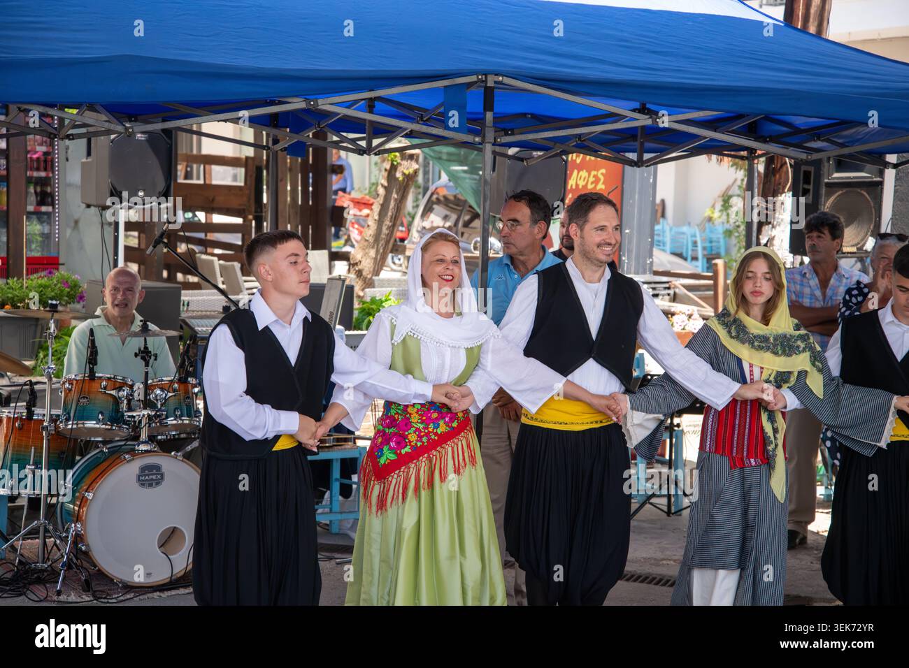 Folk dancers perform outdoor under a blue canopy wearing traditional ...