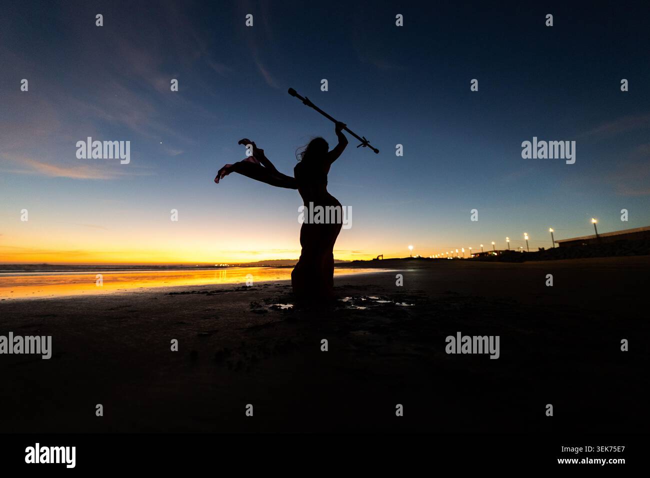 Woman in silhouette dances with a stick on a beach during sunset, with ...