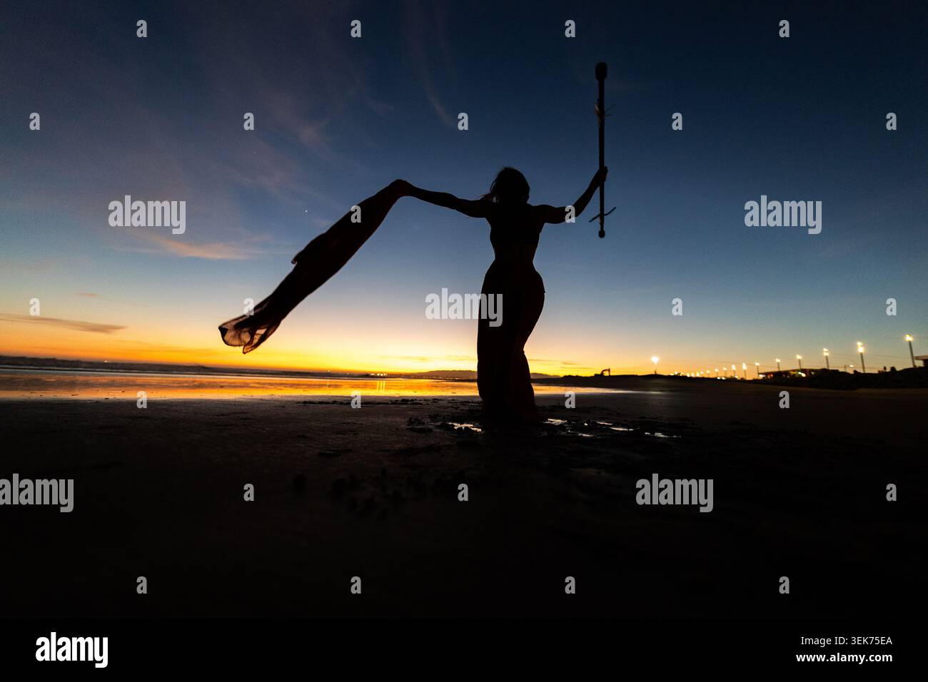 Woman's silhouette with a staff and fabric stands on the beach at ...