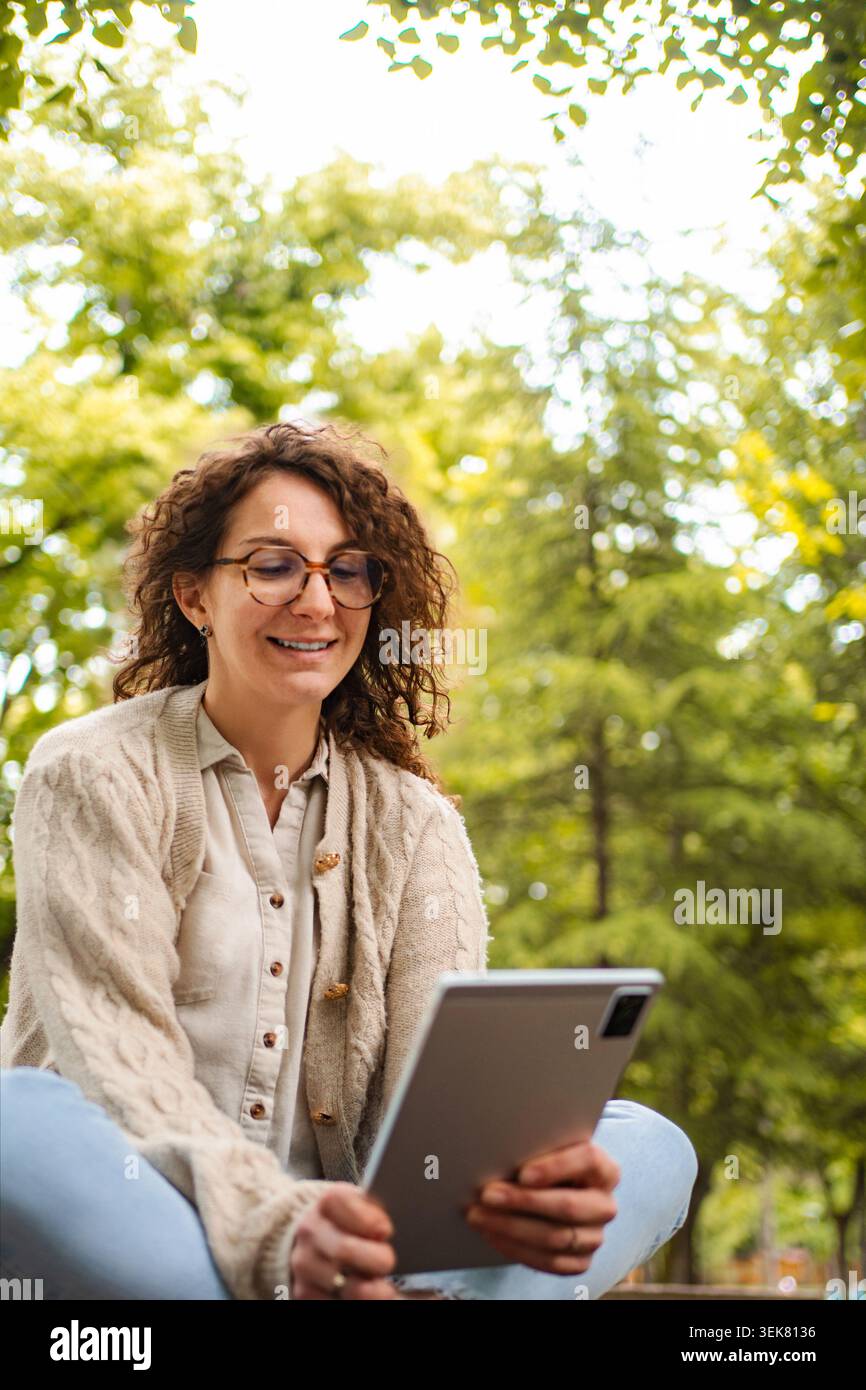 Young adult woman holding tablet computer and smiling while relaxing ...