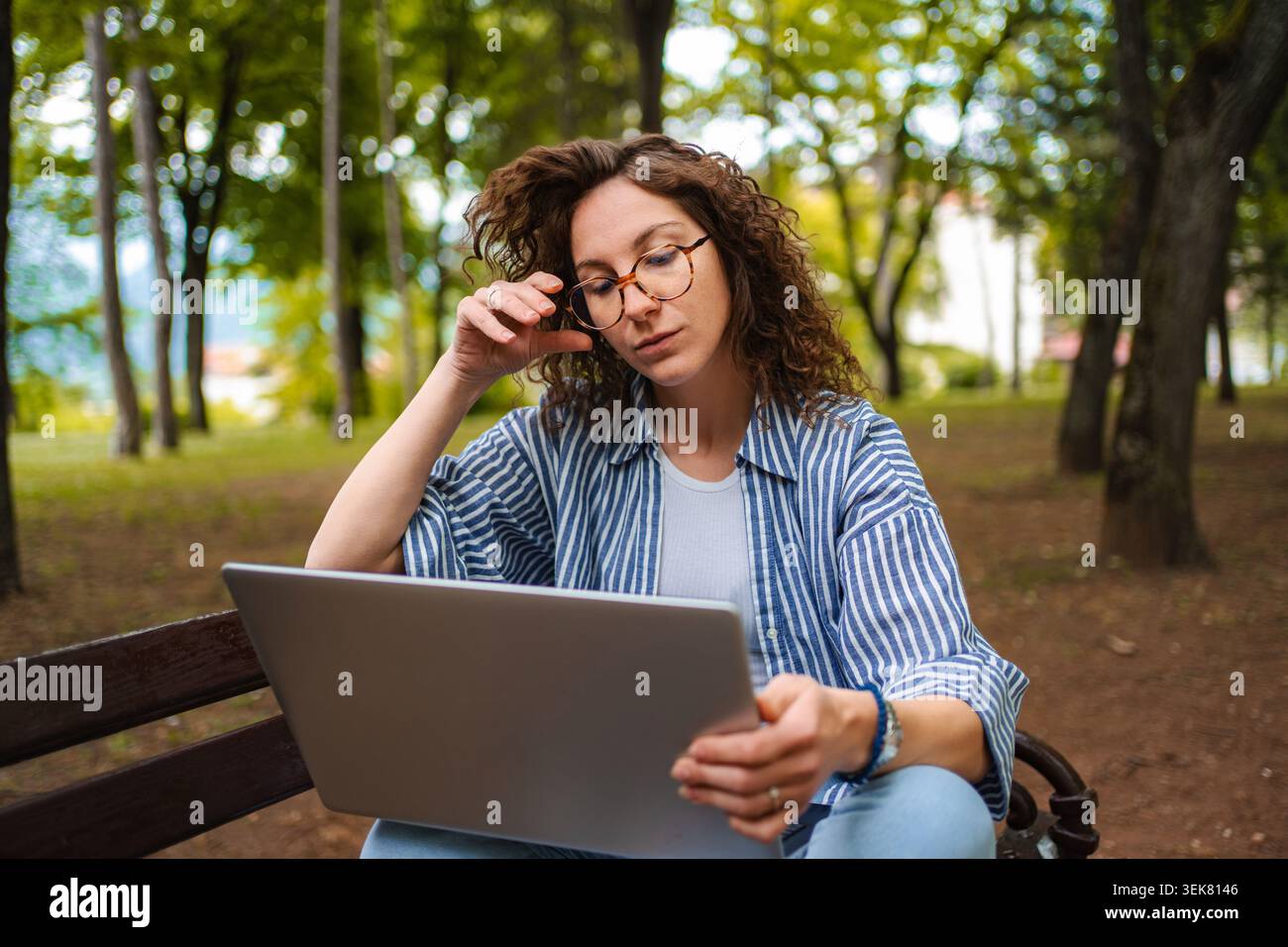 Woman focusing on work while sitting on bench using laptop in a natural ...