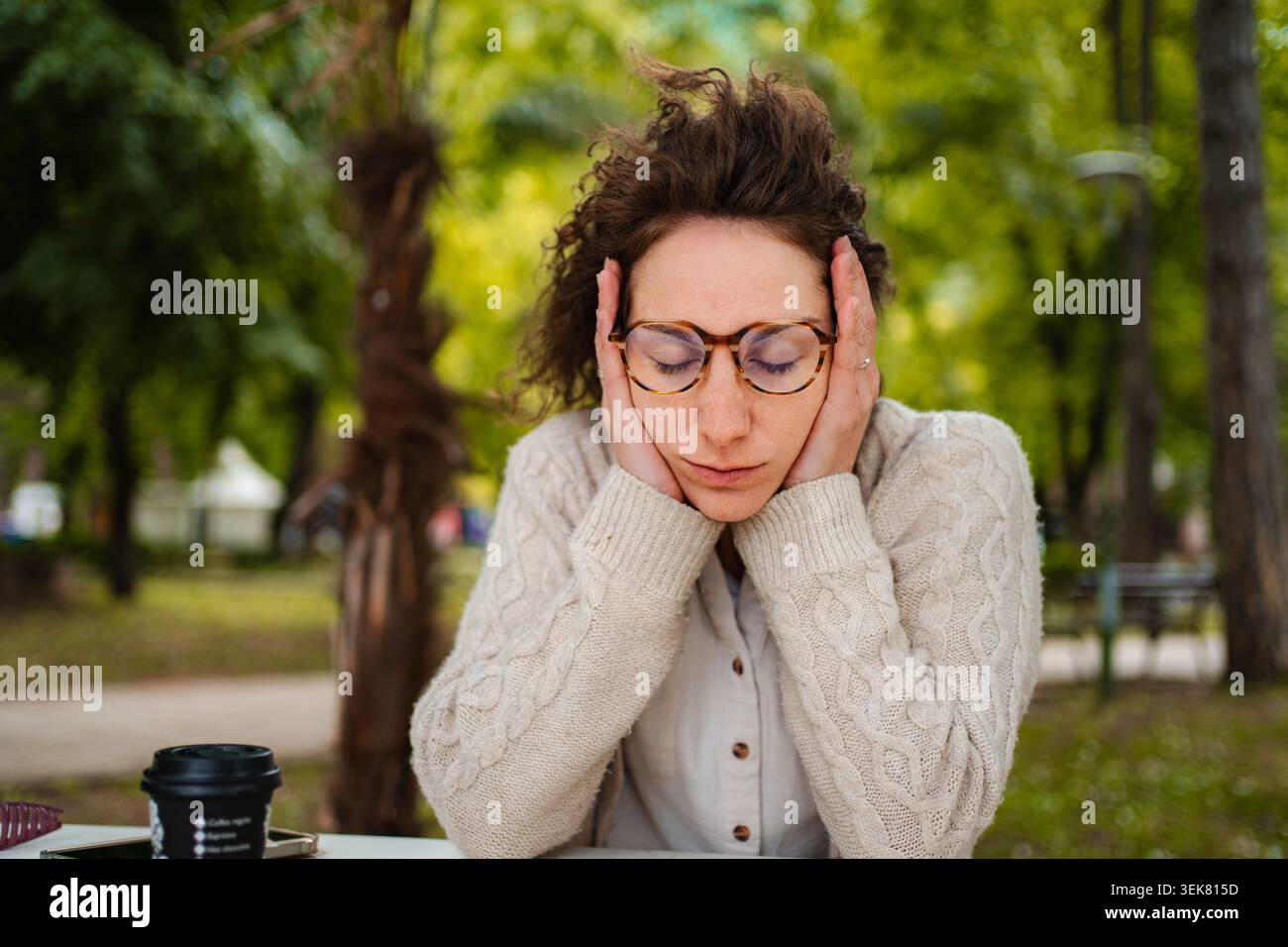 Woman feeling overwhelmed and having a headache while sitting at a park ...
