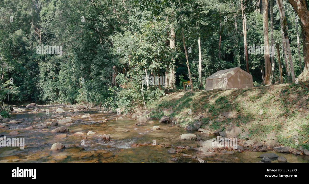 Camping tent stands on a grassy bank next to a flowing rocky river in a ...