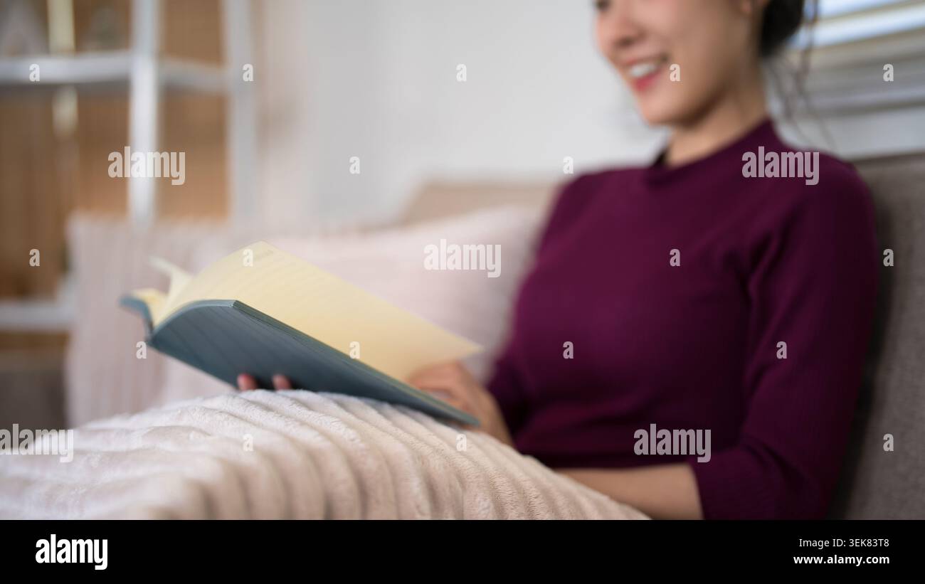 Asian woman reading book while relaxing comfortably on modern couch at ...