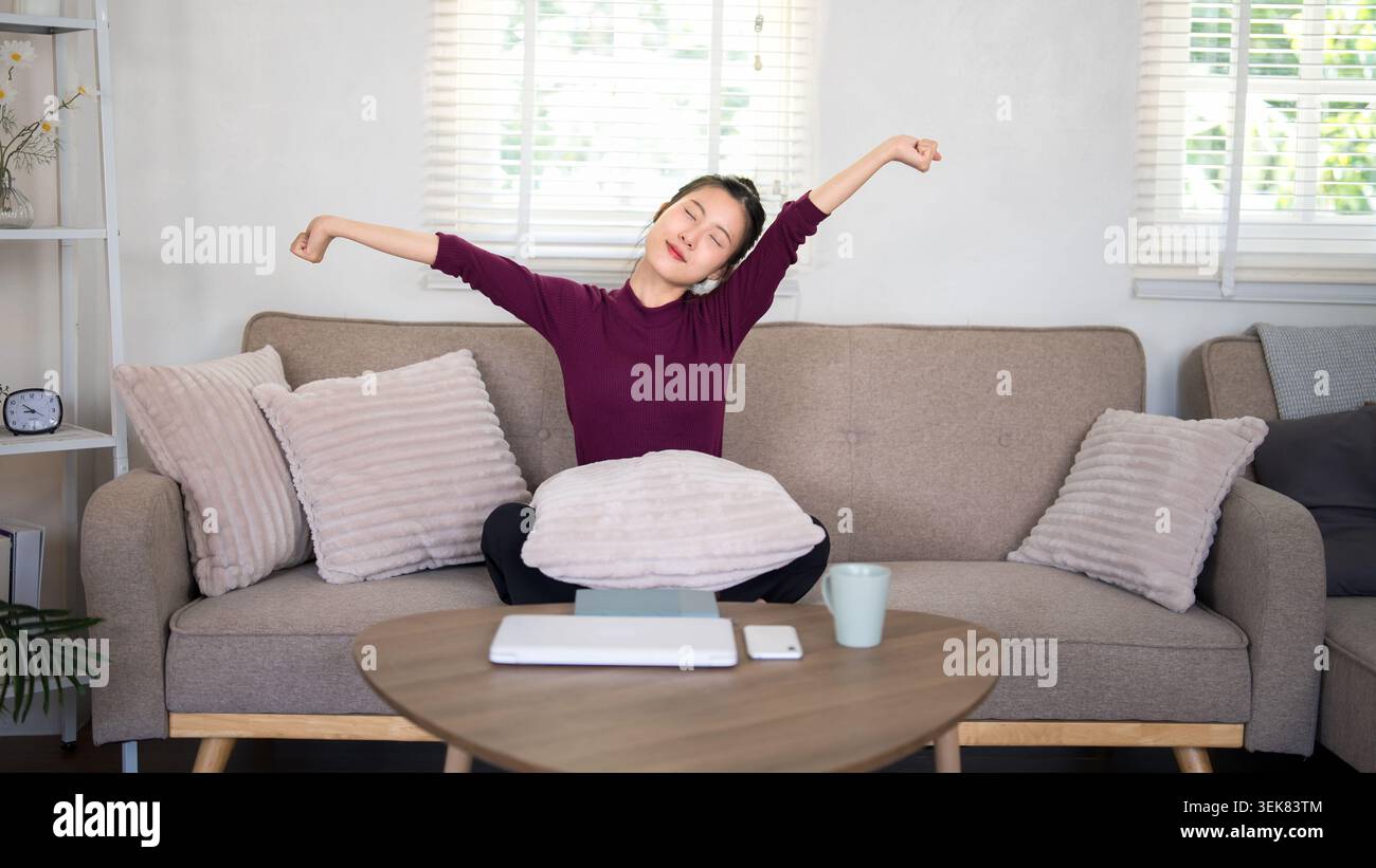 Asian women stretching arms relaxing on sofa after working from home ...