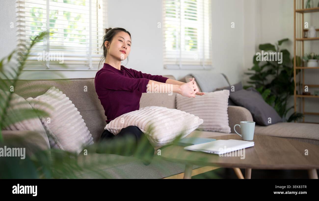 Asian women relaxing stretching arms sitting on sofa in bright living ...