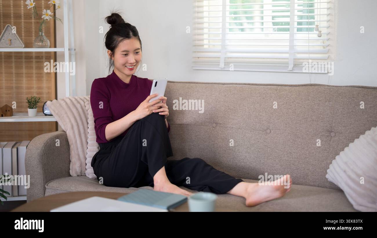 Young Asian woman using smartphone sitting on sofa relaxed casual at ...