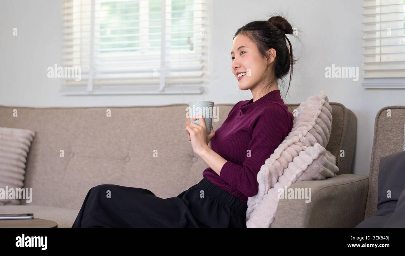 Asian woman relaxing with coffee mug at home living room taking break ...