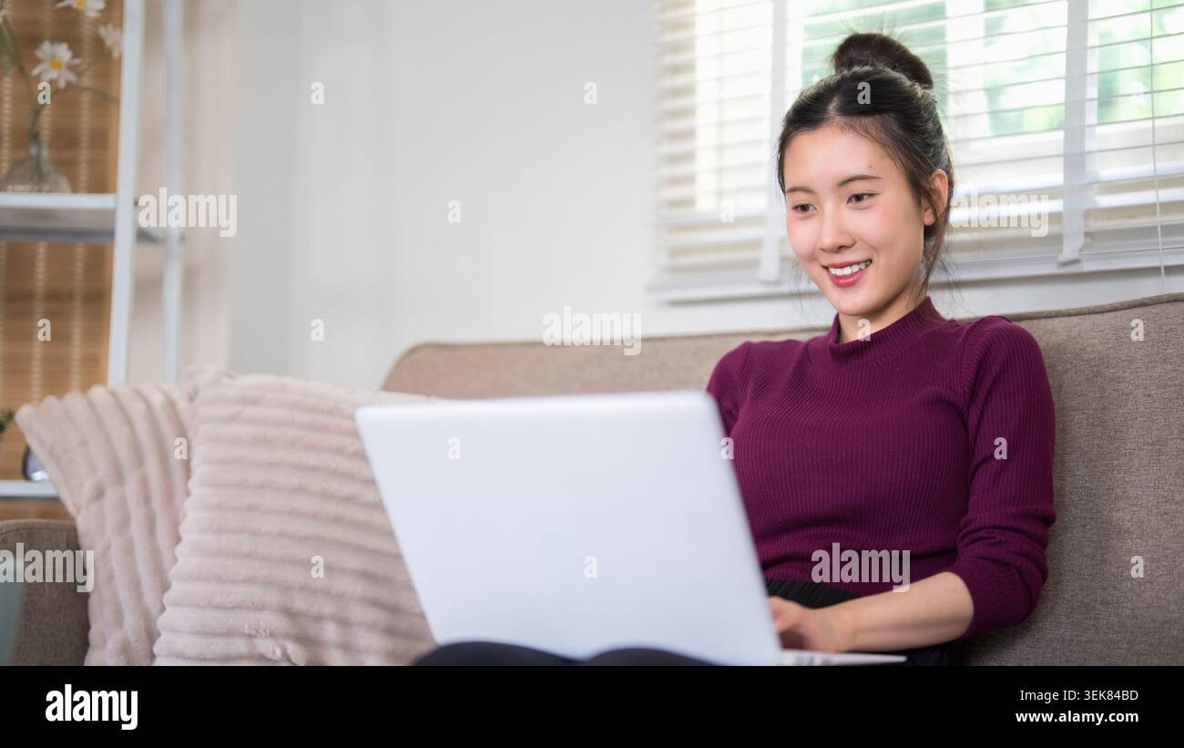 young Asian woman using laptop computer sitting on living room couch ...