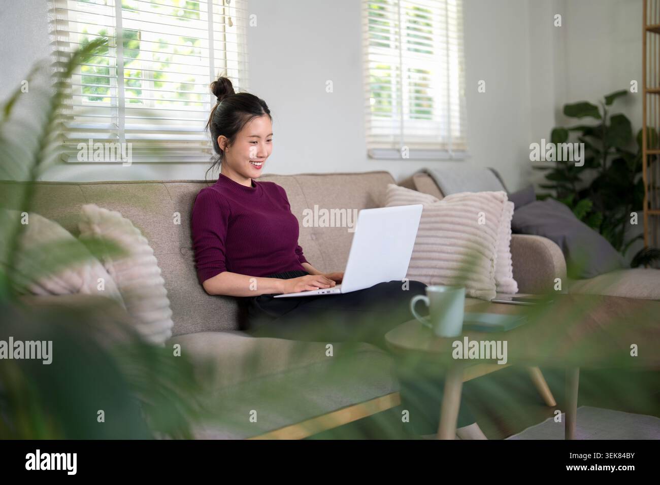 Asian women work from home using laptop computer sitting on couch in ...