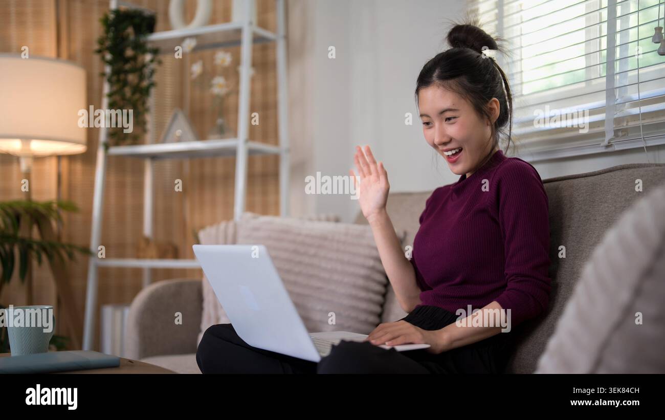 Asian woman waving during video call on laptop computer smiling happy ...