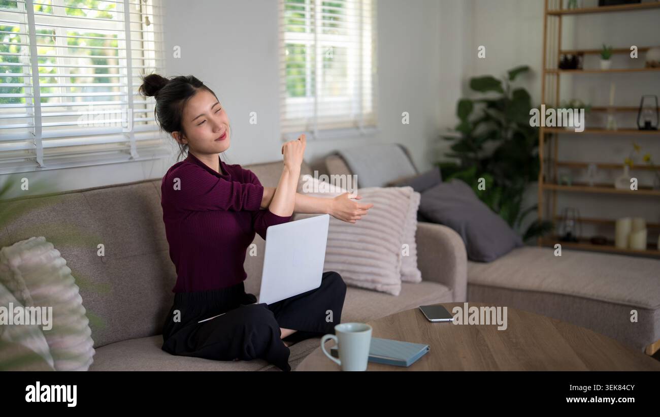 Asian woman stretching arms while sitting on sofa at bright modern home ...
