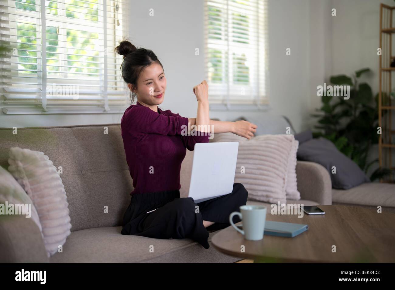 young Asian woman celebrating work success sitting on sofa with laptop ...
