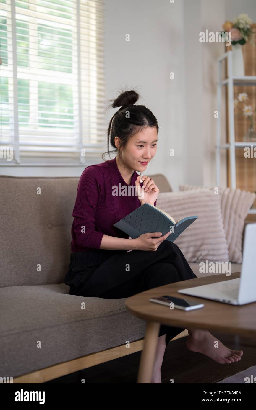 Asian woman reading book studying on comfortable sofa at home living ...