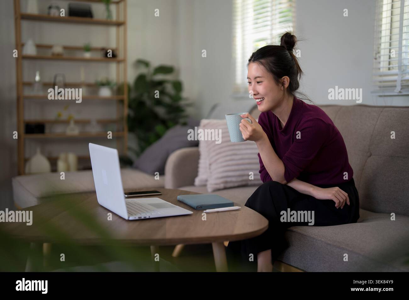 Young Asian woman smiling using laptop drinking beverage at home office ...