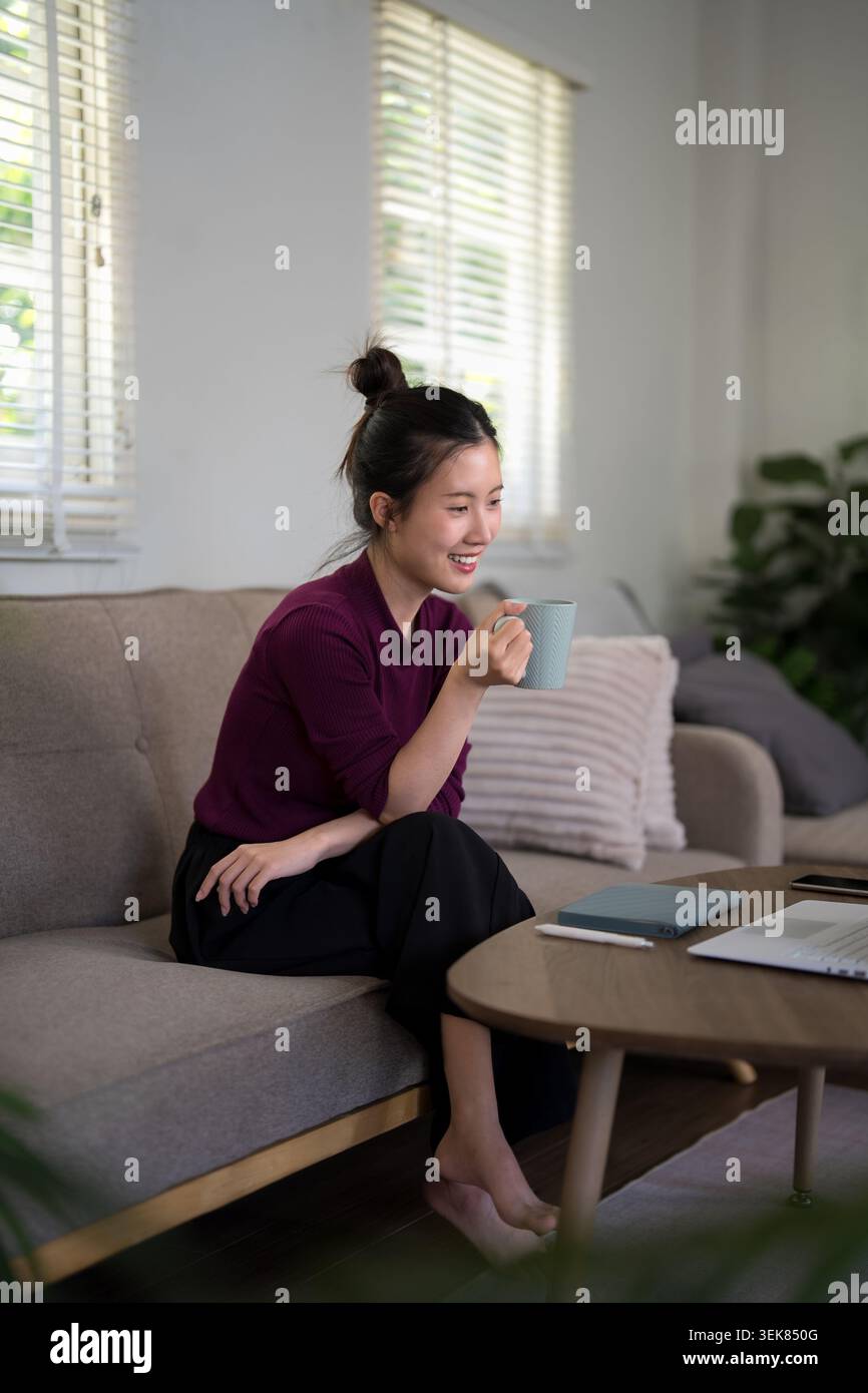 Asian women relaxing on sofa drinking coffee at home in modern bright ...