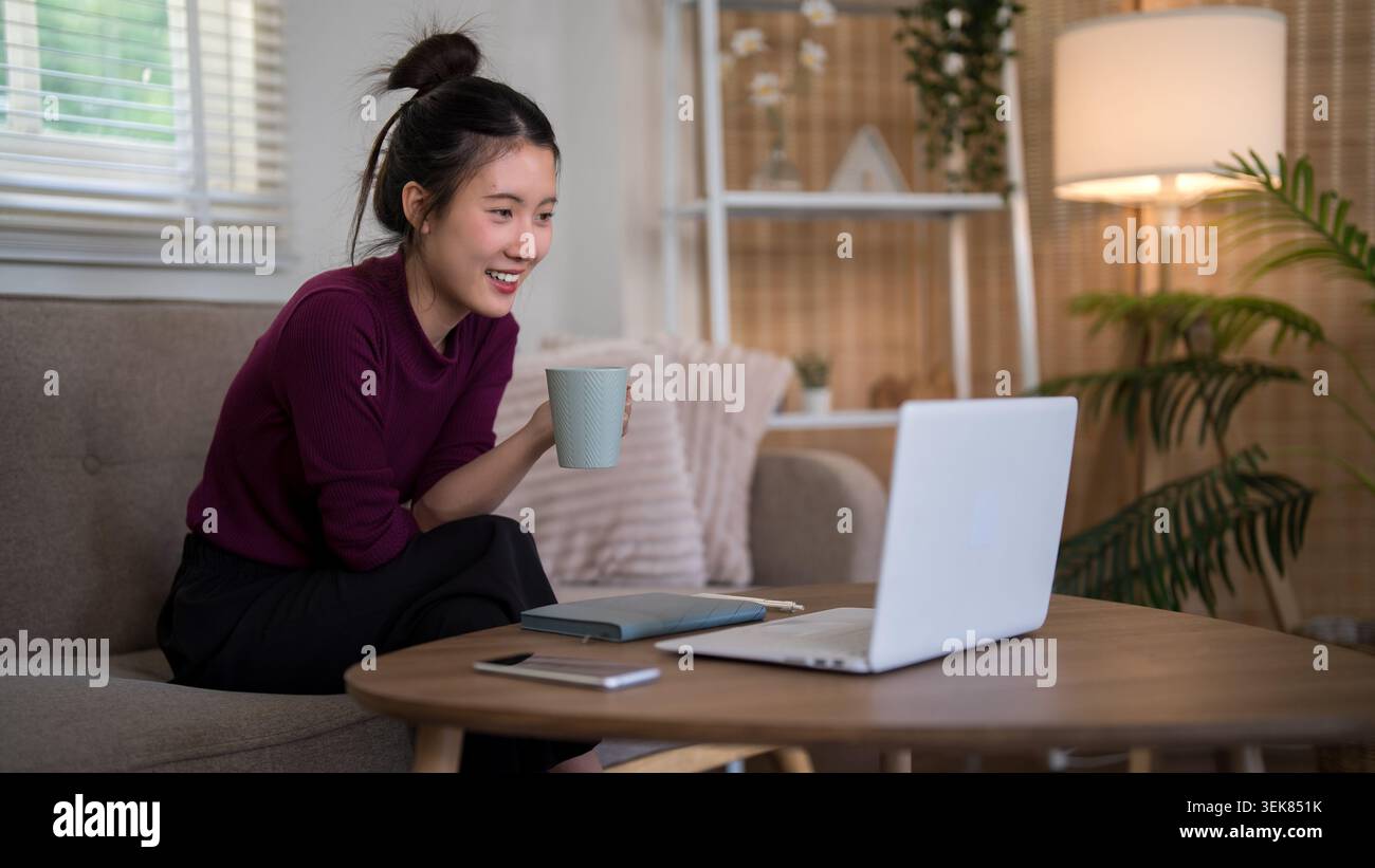Asian adult woman holding coffee mug using laptop computer smiling ...