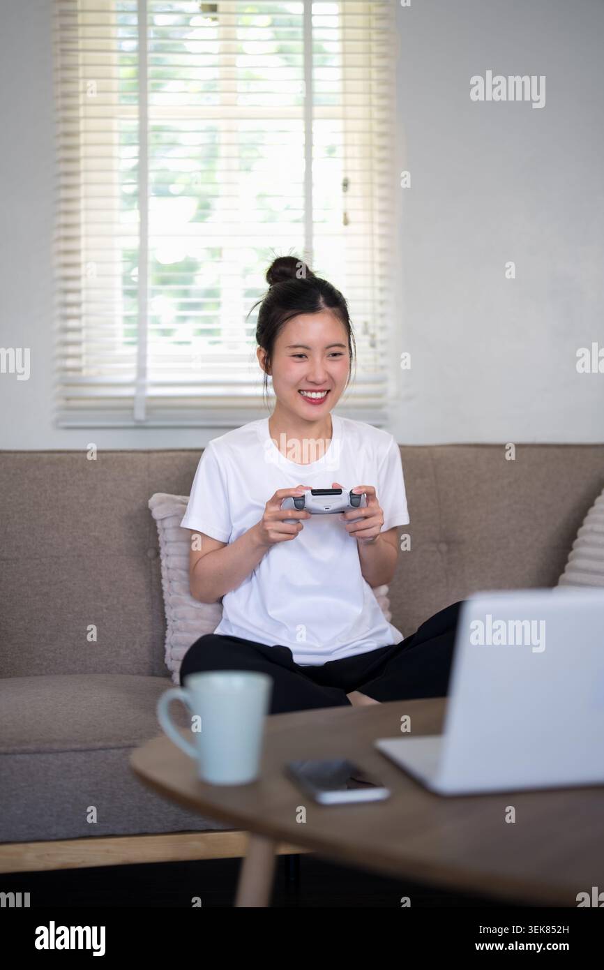 young Asian woman enjoying mobile gaming on smartphone while relaxing ...