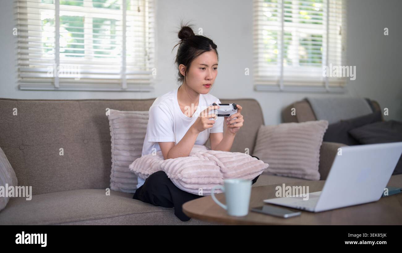Asian woman relaxing on sofa with coffee cup and laptop in bright ...