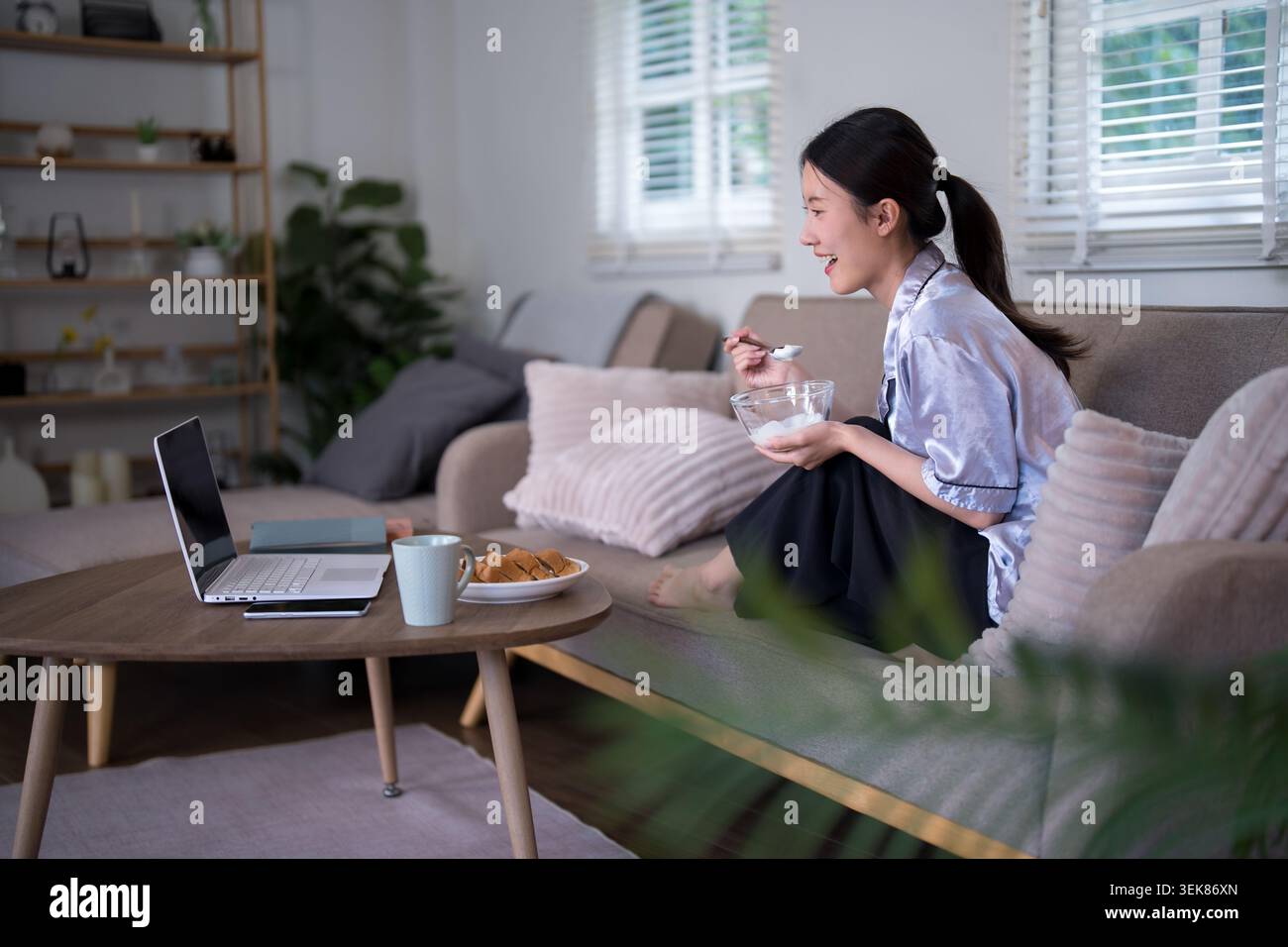 Young Asian woman enjoying healthy breakfast while using laptop ...