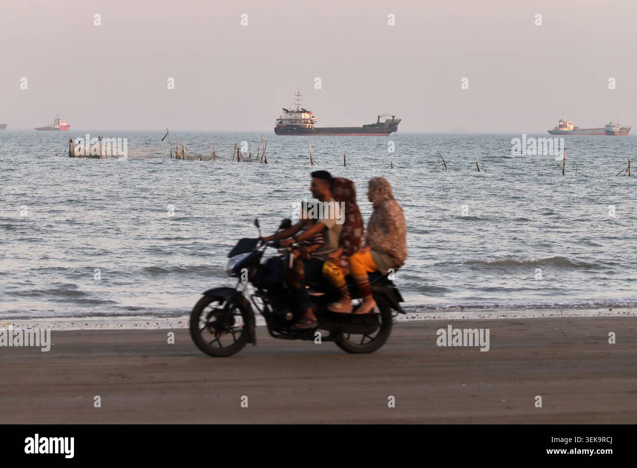 Cargo and service vessels line the horizon as people ride a motorcycle ...