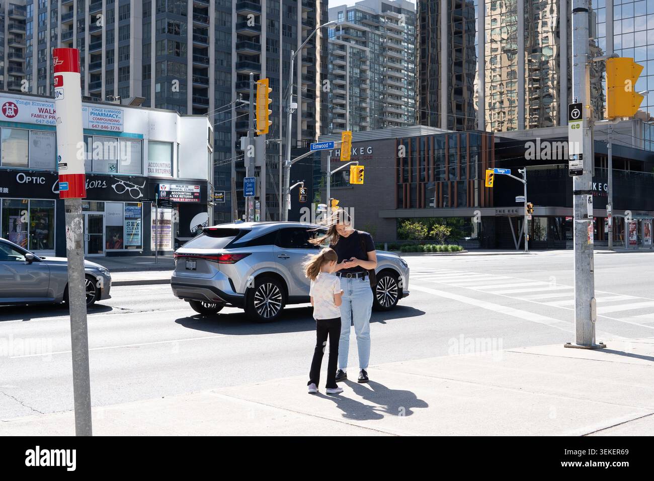 A woman and a young girl stand on a city sidewalk at a busy ...