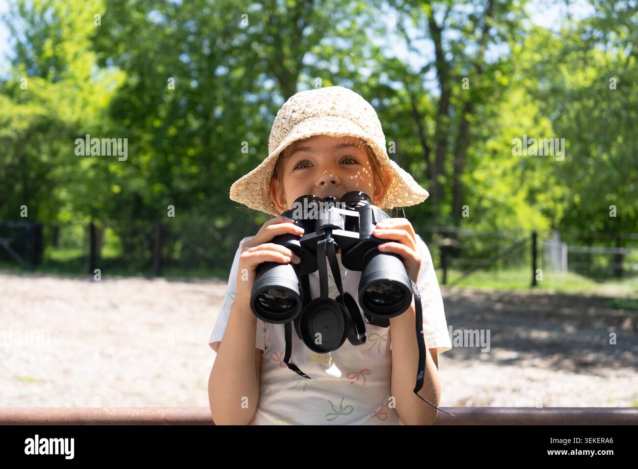 A young girl wearing a straw hat holds a pair of binoculars while ...