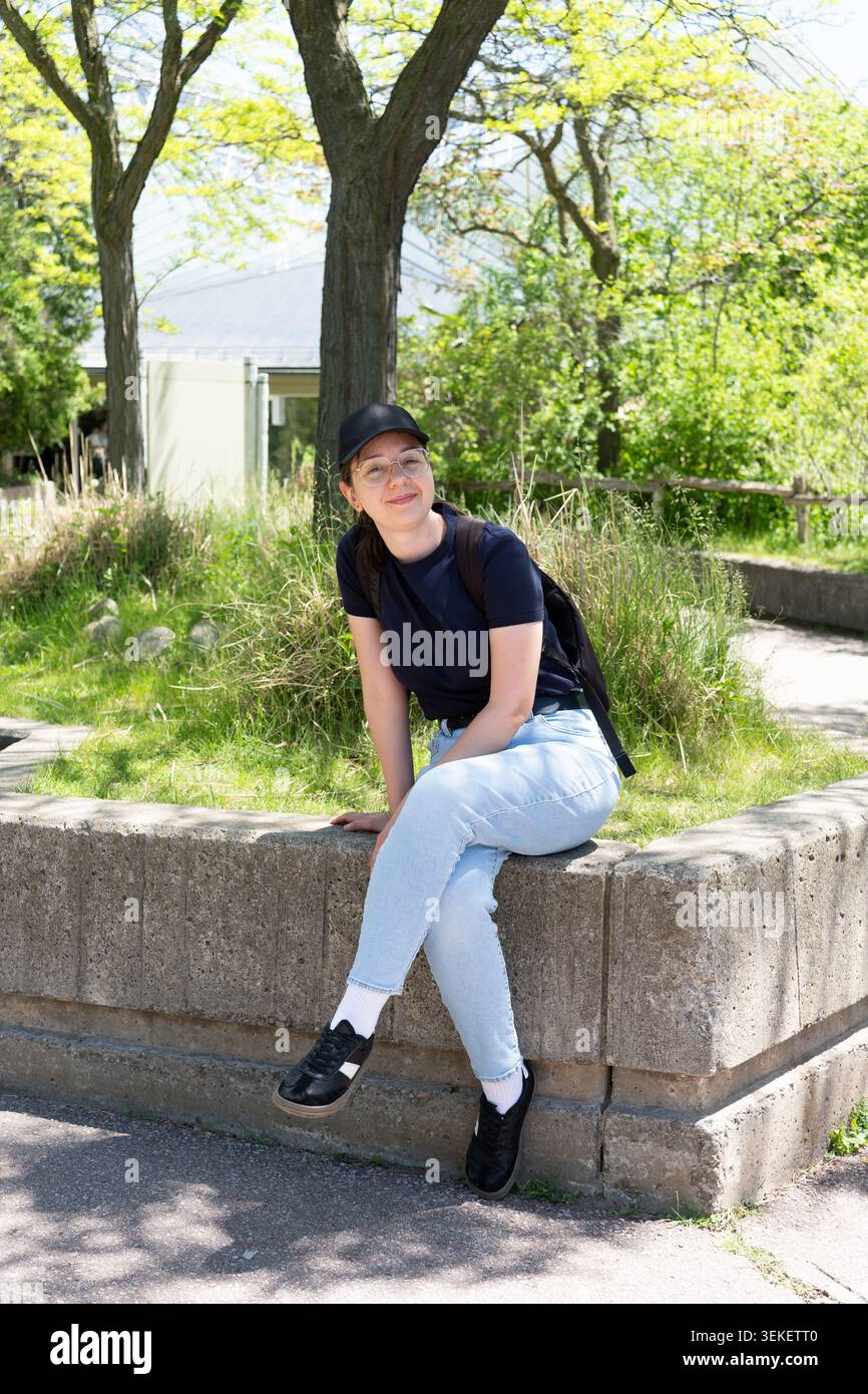 A young woman wearing glasses, a black cap, navy t-shirt, light blue ...