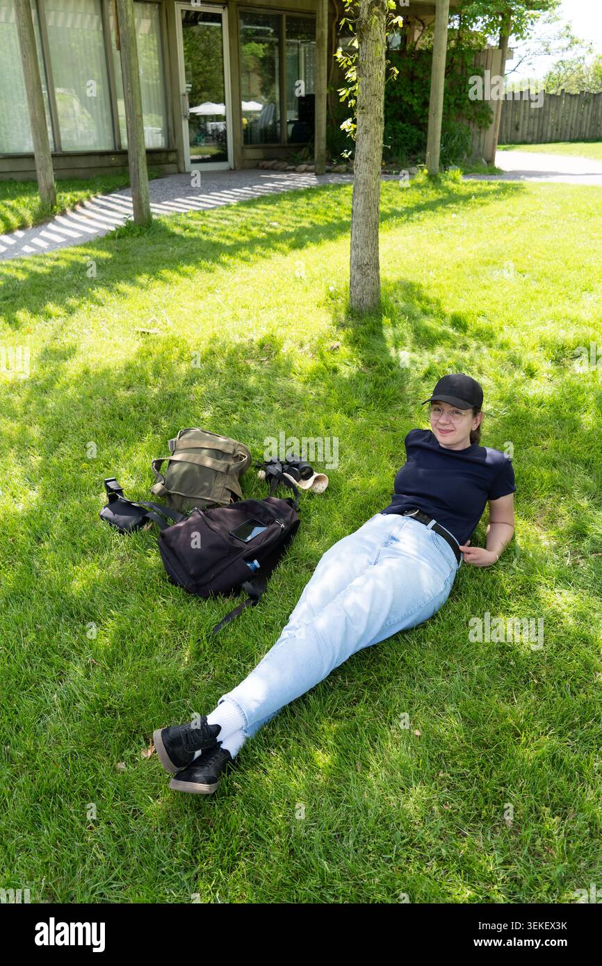 A young woman in a black cap and glasses relaxes on green grass in the ...