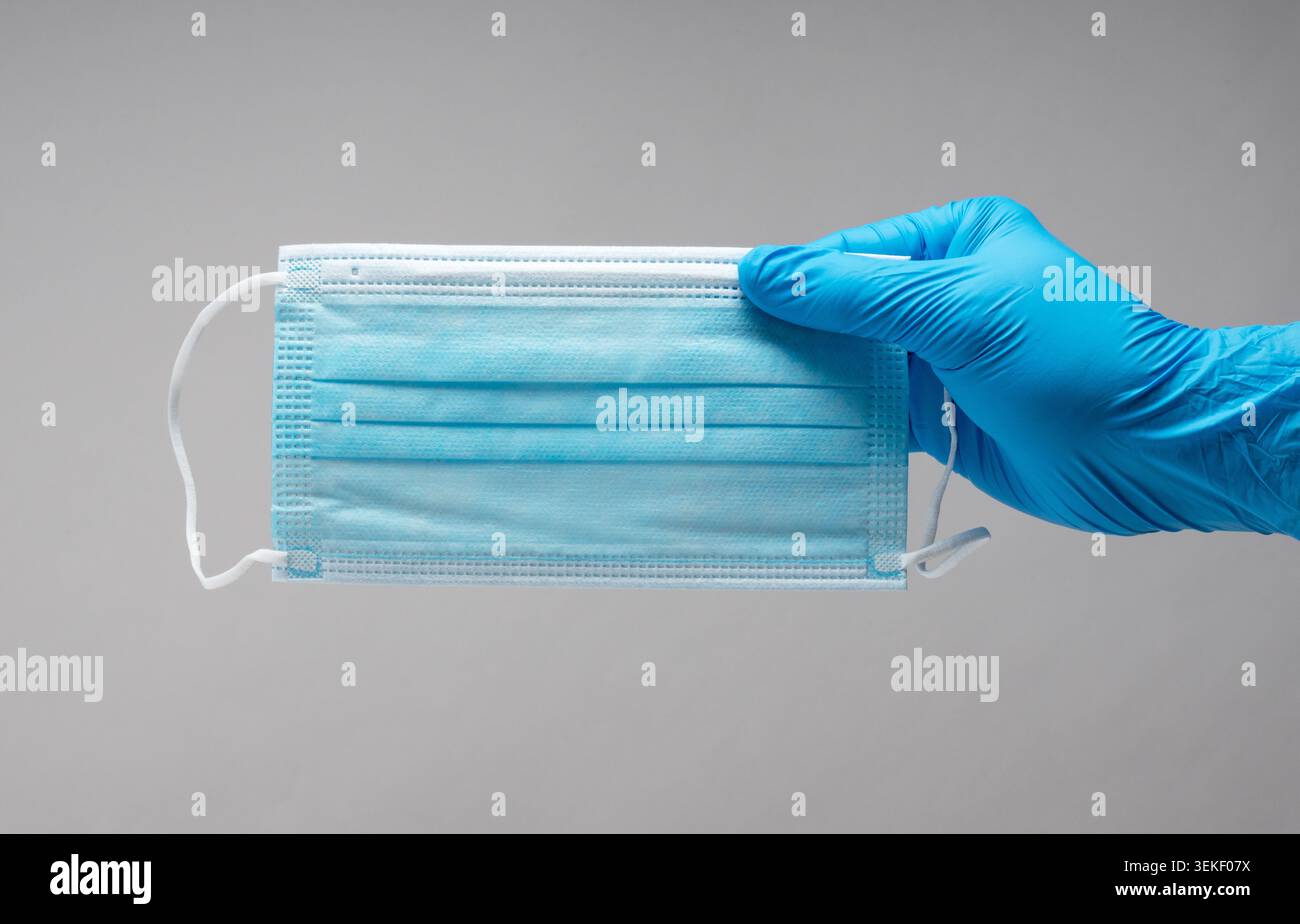 Gloved Hand Holding Blue Disposable Surgical Face Mask on Gray ...