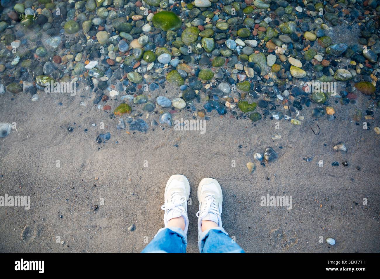 Person standing near transparent sea water with colorful stones on ...