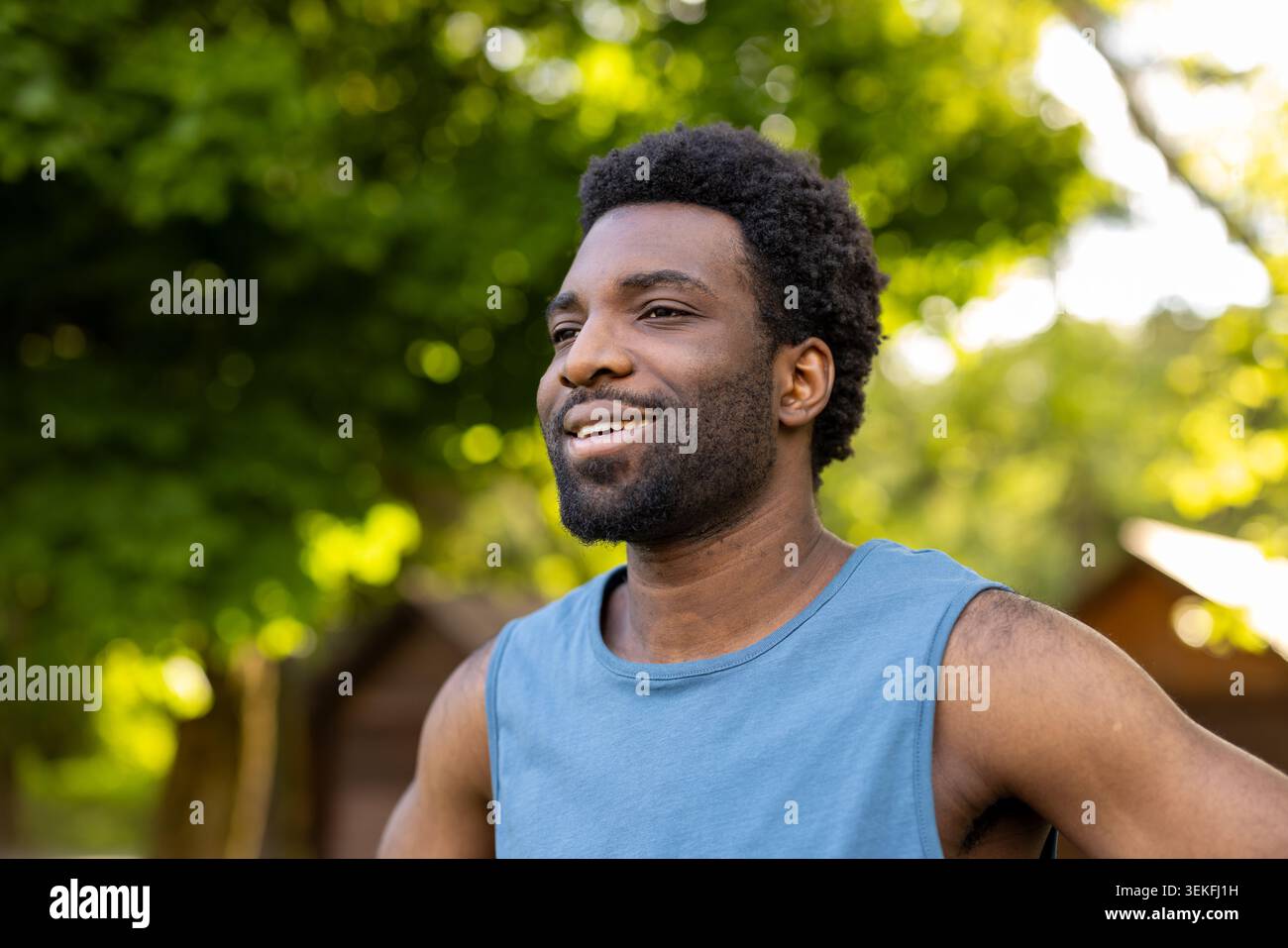 Young man standing outdoors in a park, smiling and looking away ...