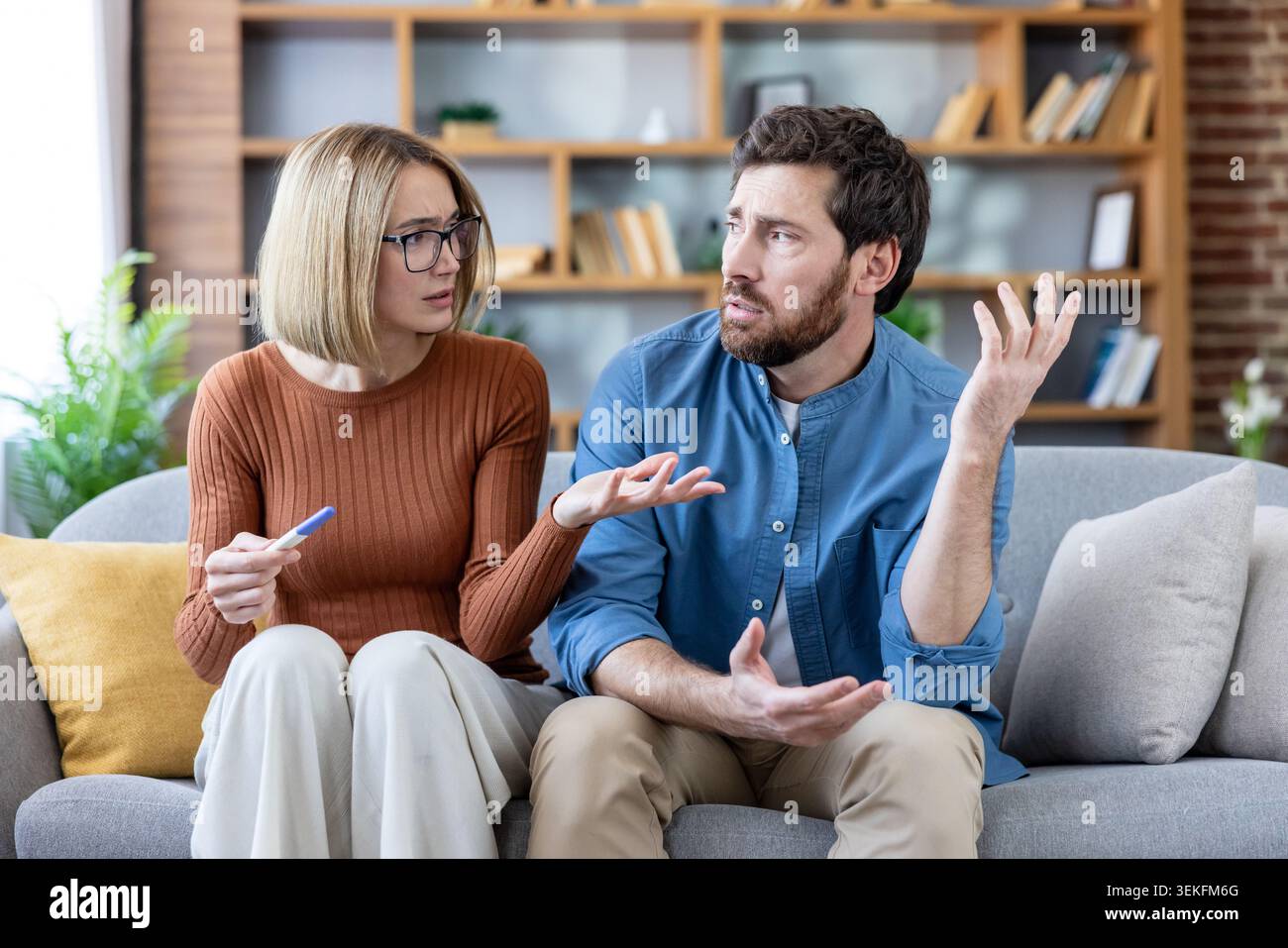 Concerned woman sitting on a sofa holding a positive pregnancy test and ...