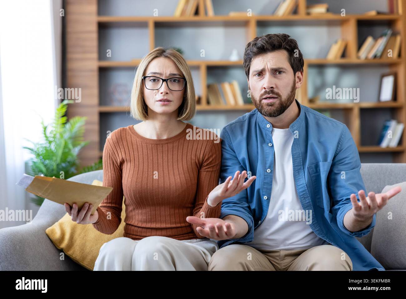 Shocked young couple sitting on a sofa in their living room, looking at ...