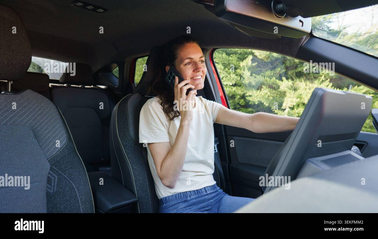 Woman driving and smiling while talking on a mobile phone in a car ...