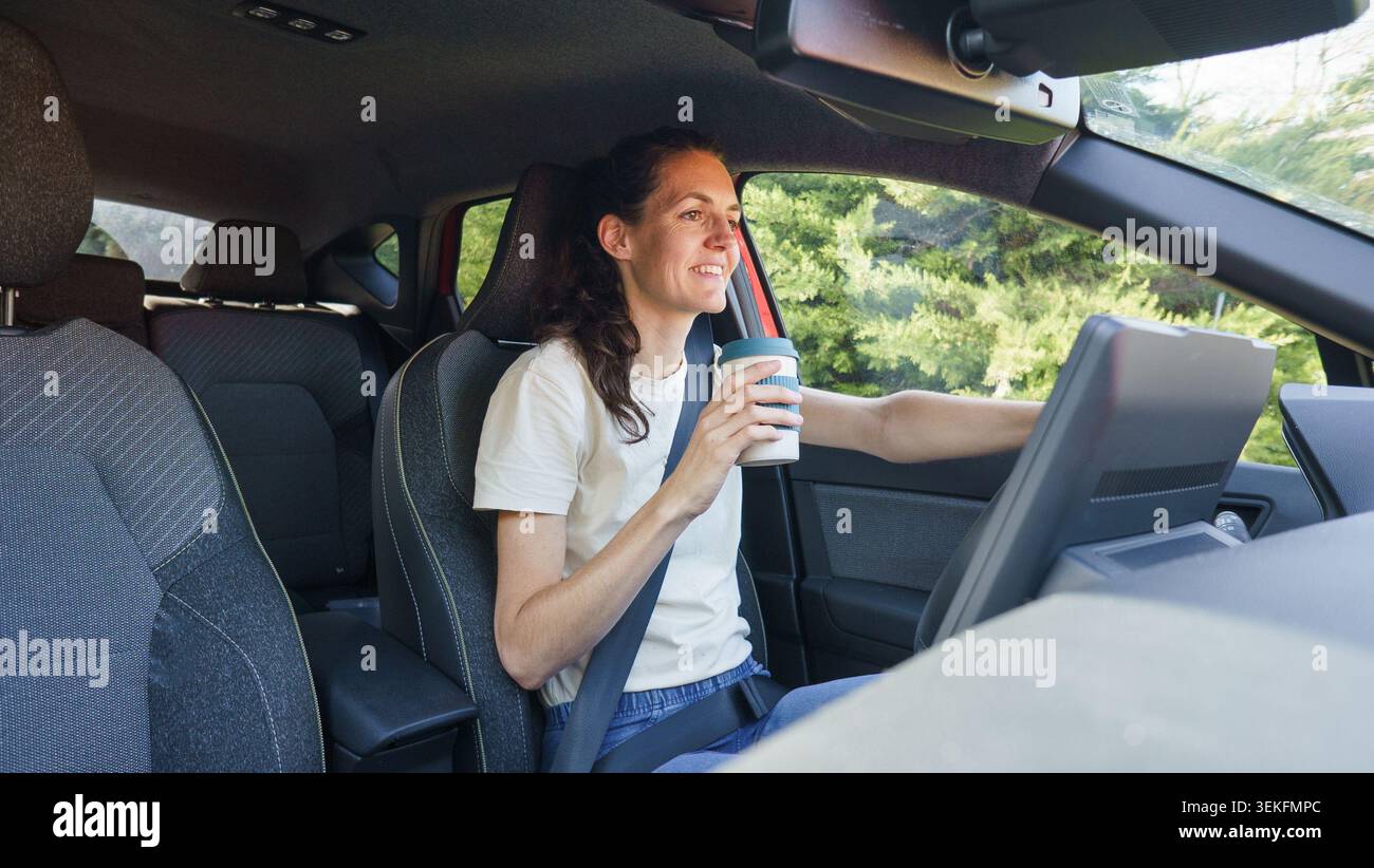 Woman smiling inside car, wearing seatbelt and holding a coffee cup ...