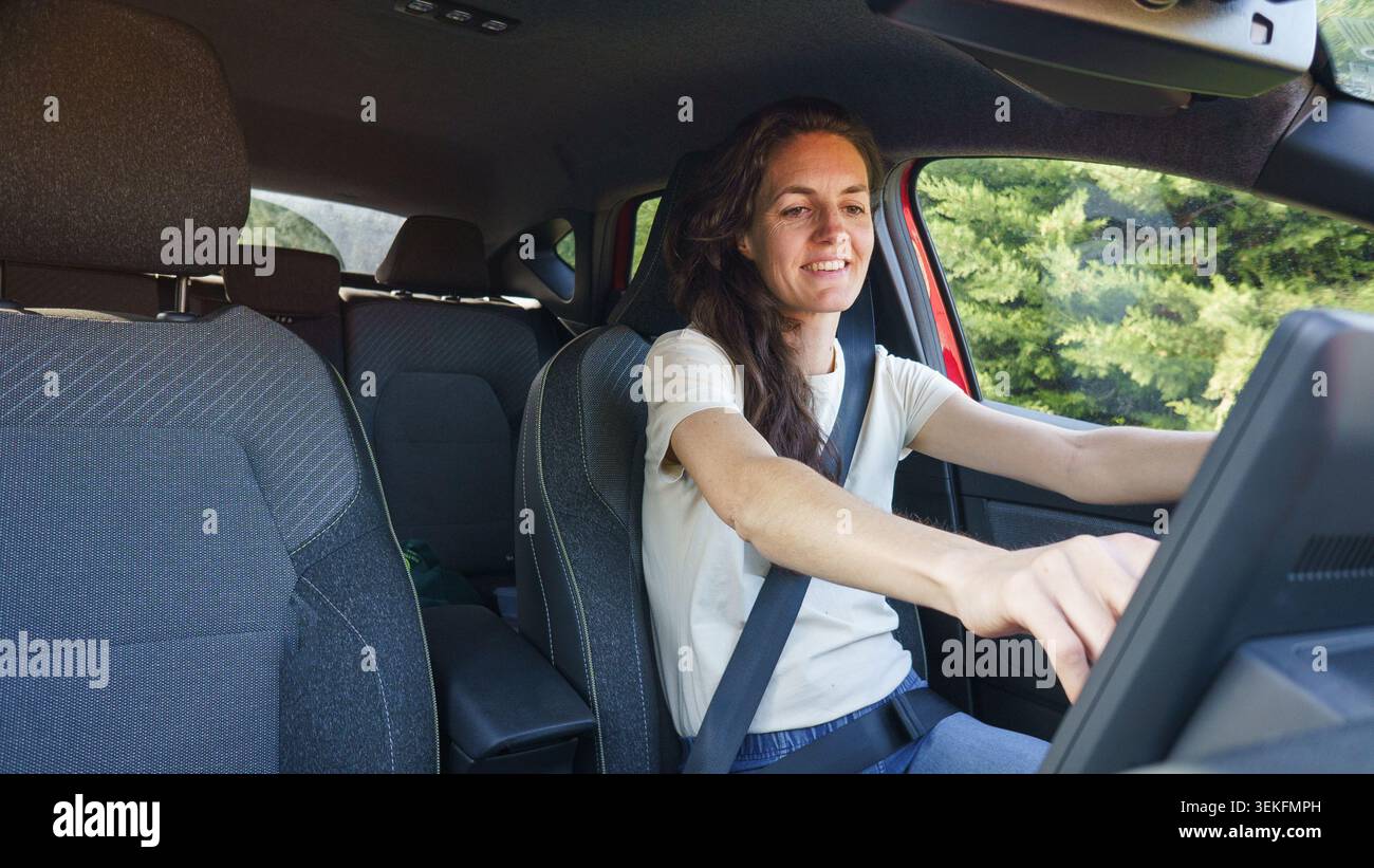 Young woman driving vehicle, interacting with touch screen display on ...