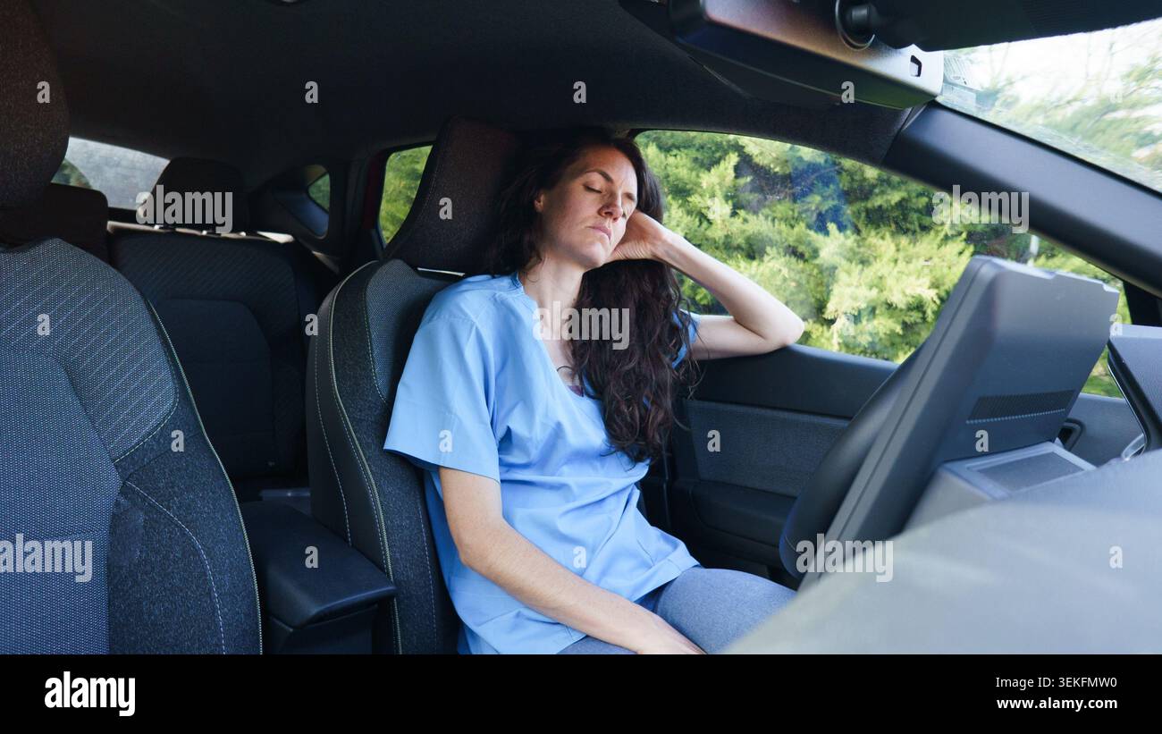 Healthcare professional wearing blue scrubs napping inside a vehicle ...