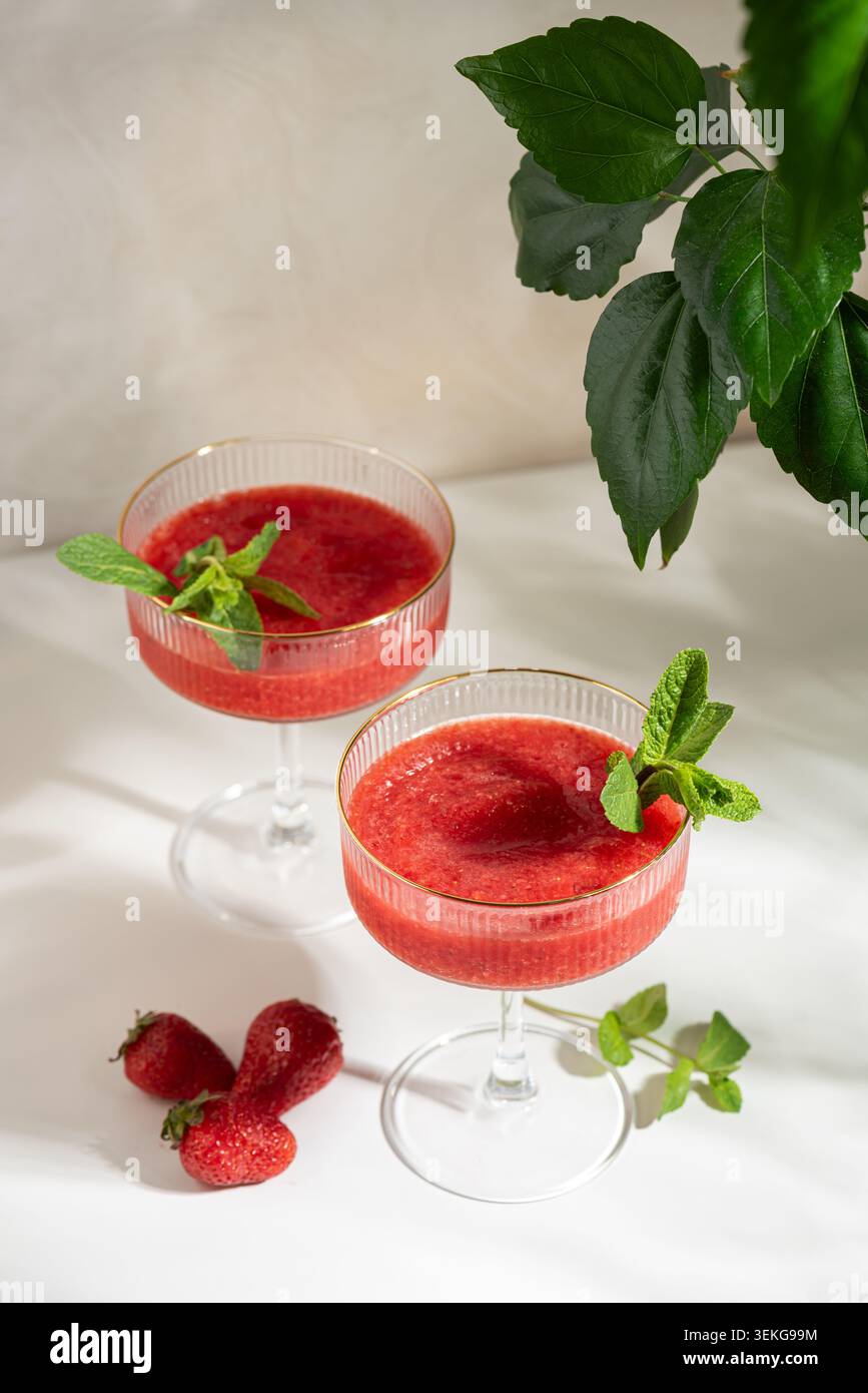 Two glasses of sweet strawberry frozen cocktails with mint garnish on a ...
