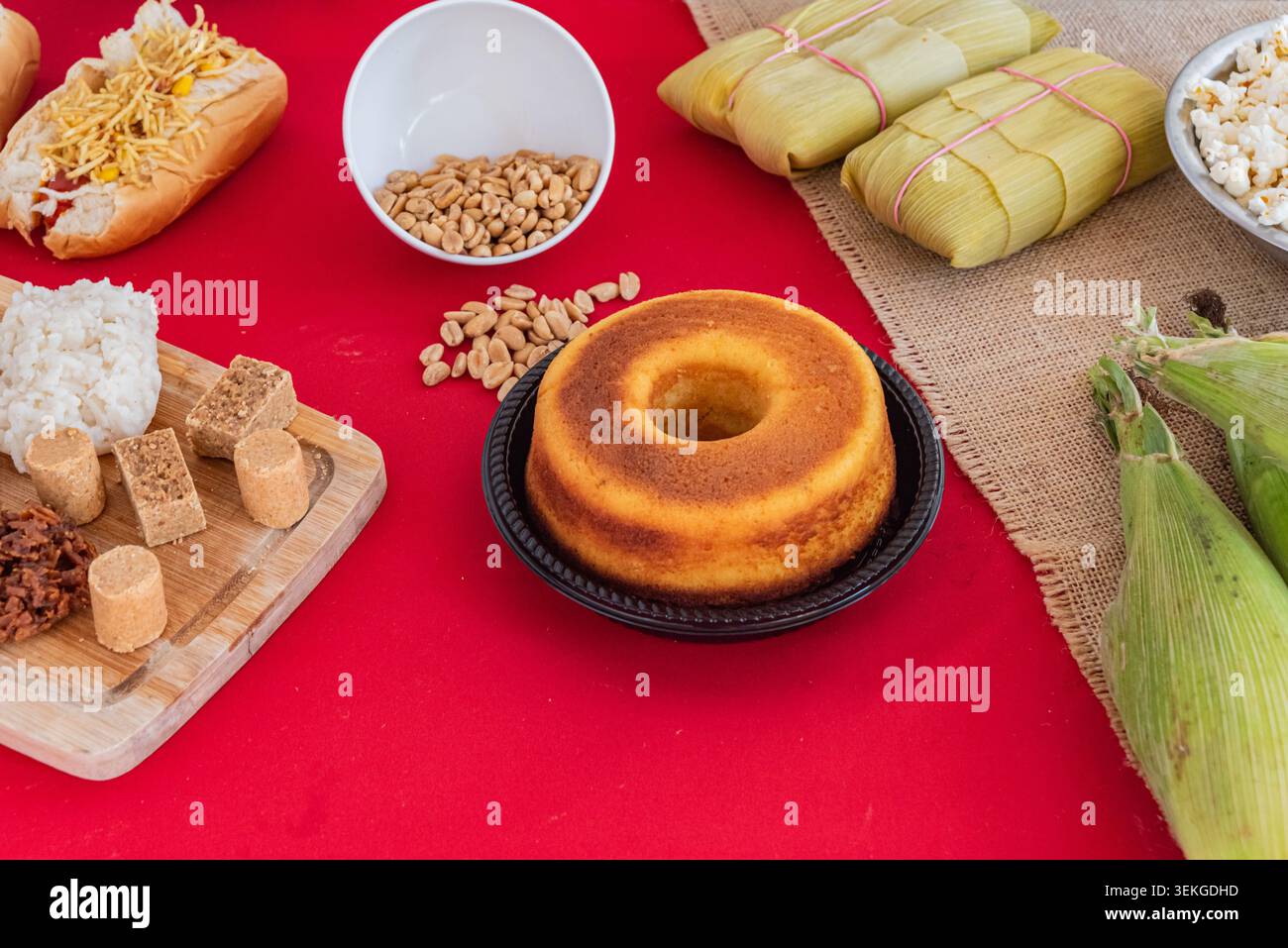 Still life featuring corn cake, peanuts, and corn on red surface ...