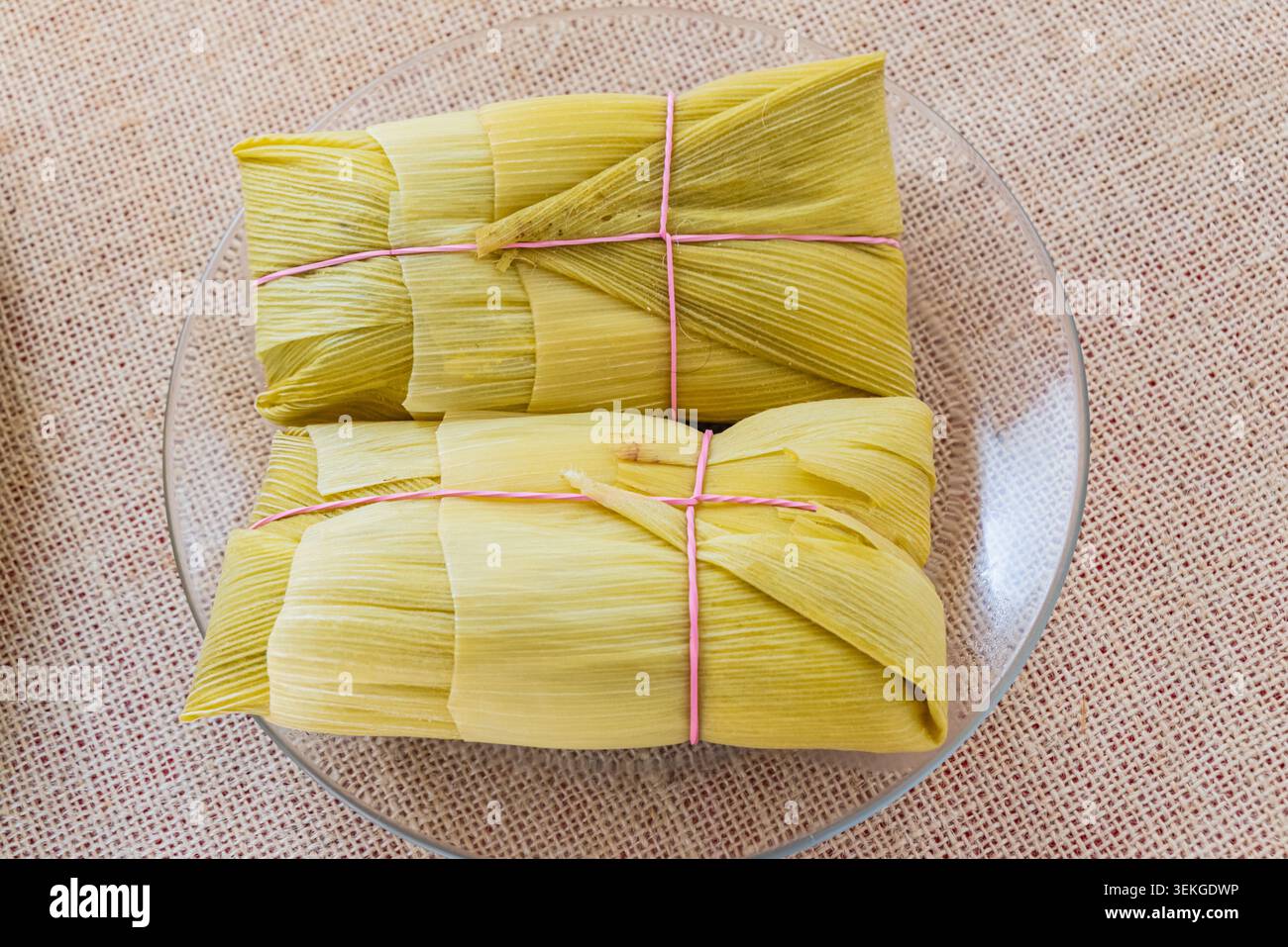 Two pamonhas wrapped in corn husks and tied with pink string on glass ...