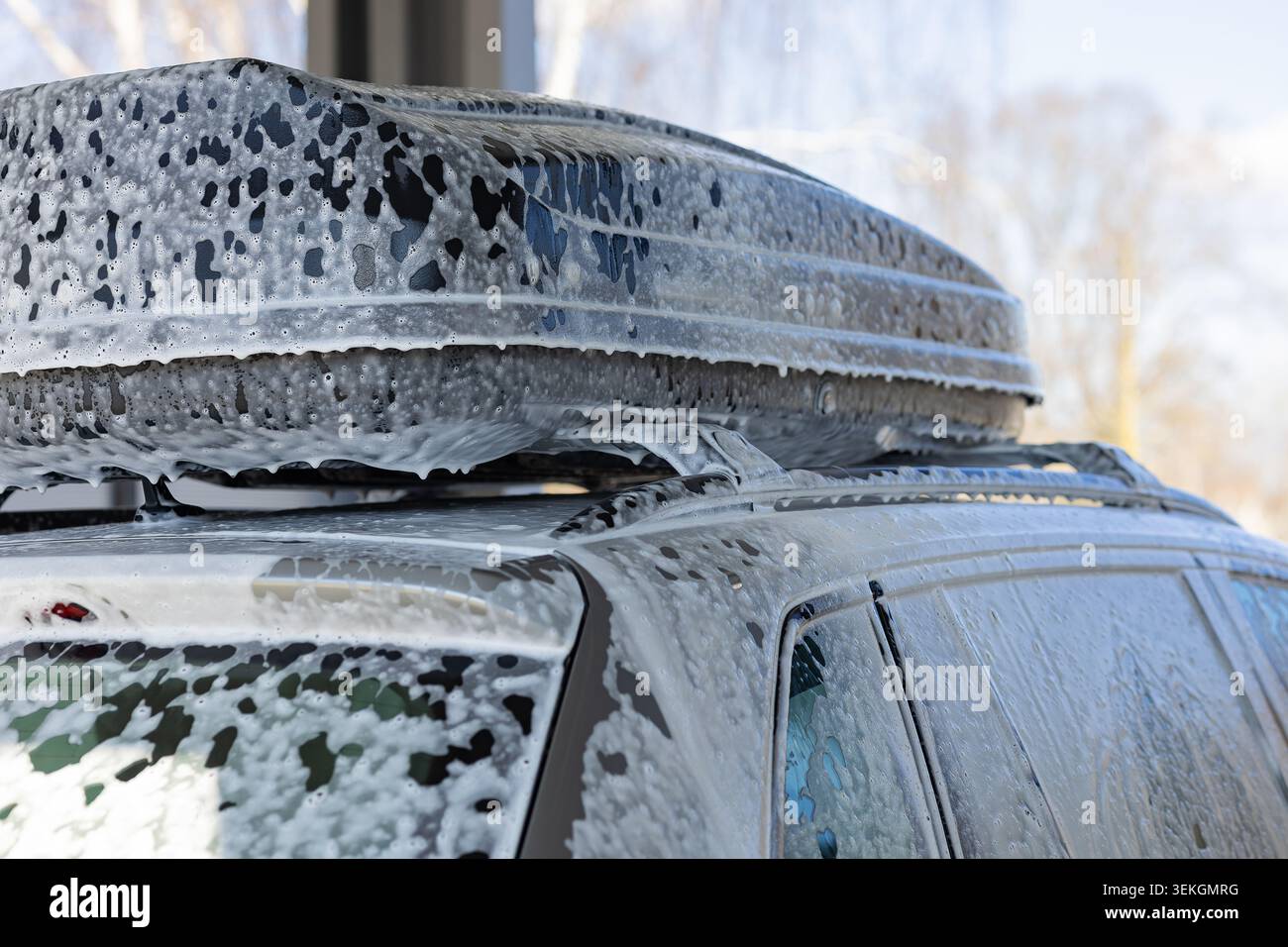Modern car with black roof box covered in active white soap foam during ...