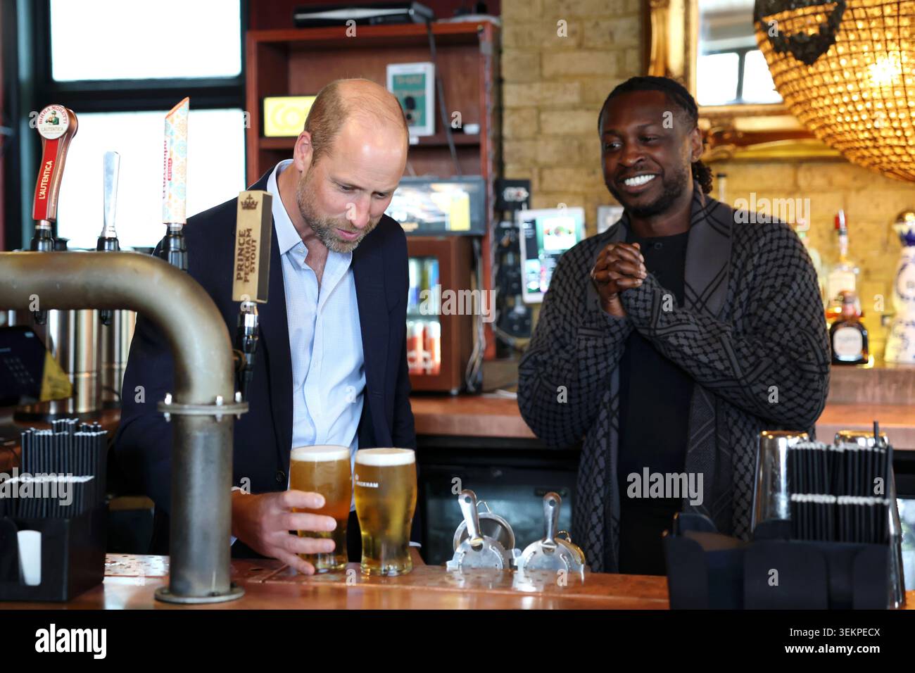 The Prince of Wales pours a pint alongside Clement Ogbonnaya during a ...