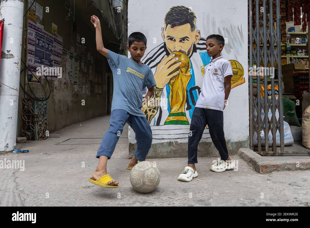 Two boys seen playing foot ball in front of a graffiti of famous ...